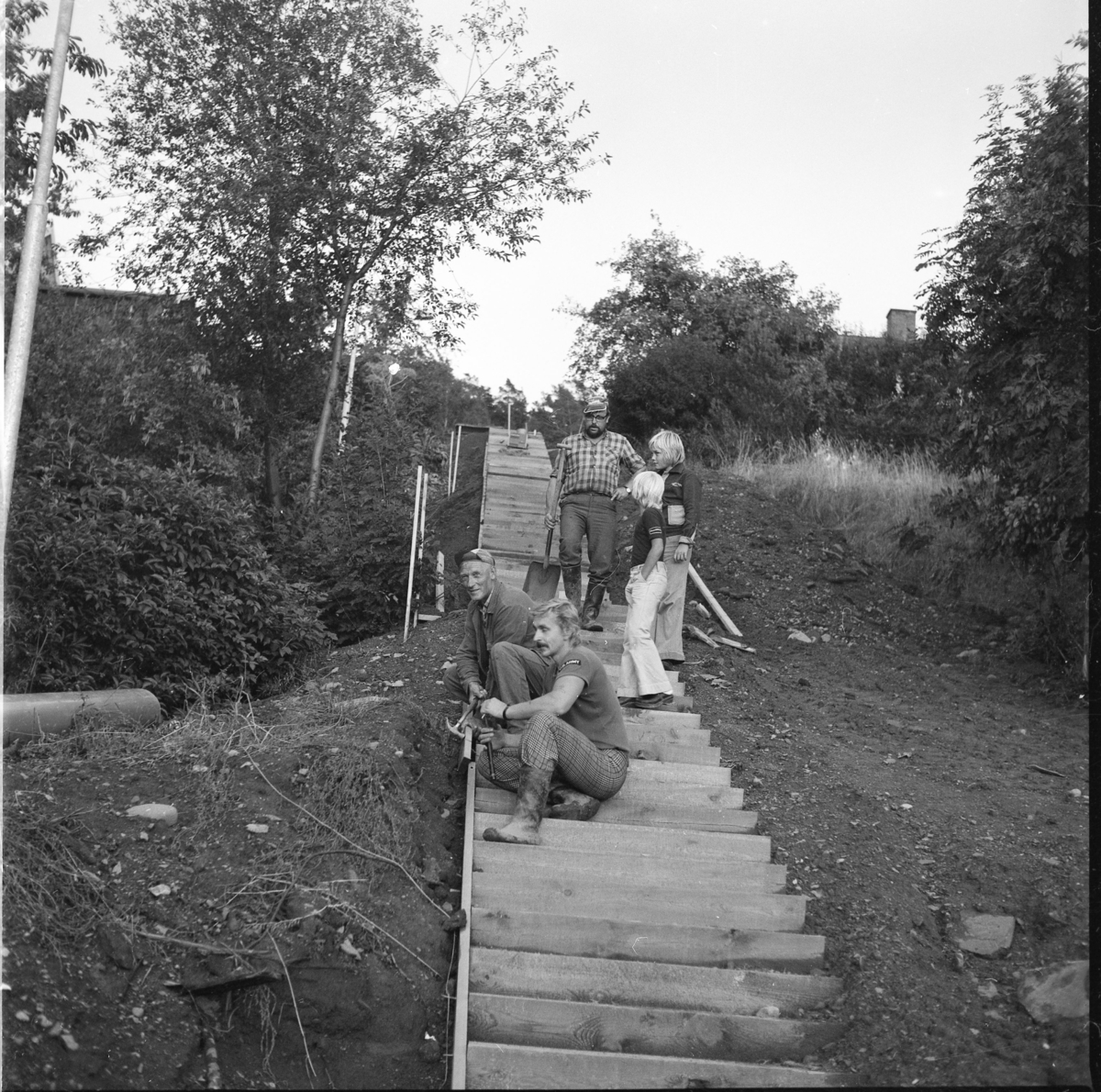 Två män snickrar på en lång trappa. Två pojkar står intill och tittar ...