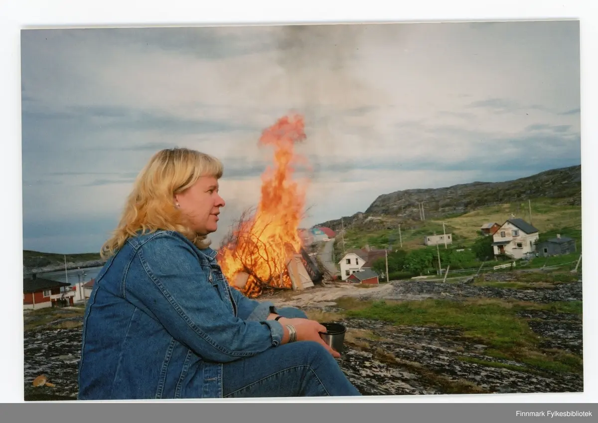 Anne Ulven sitter på gressbakken med kaffekoppen. St.Hansbålet i ...