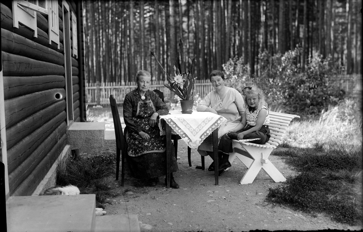 Gruppebilde.Ved et bord i hagen sitter mor til Alma,Alma og Gard ...