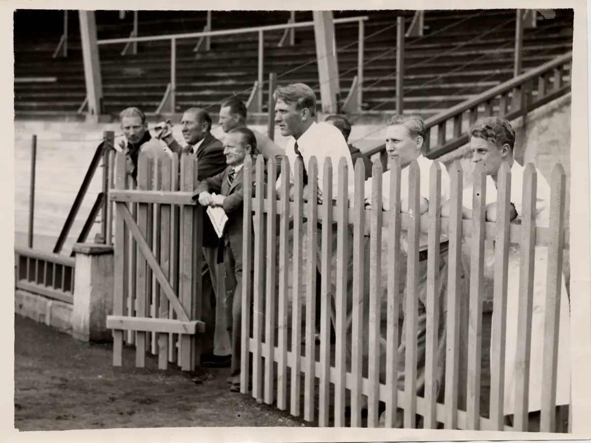 Åtta män står bakom en grind, 1940-talet. Slottsskogsvallen. 2:e fr.h ...