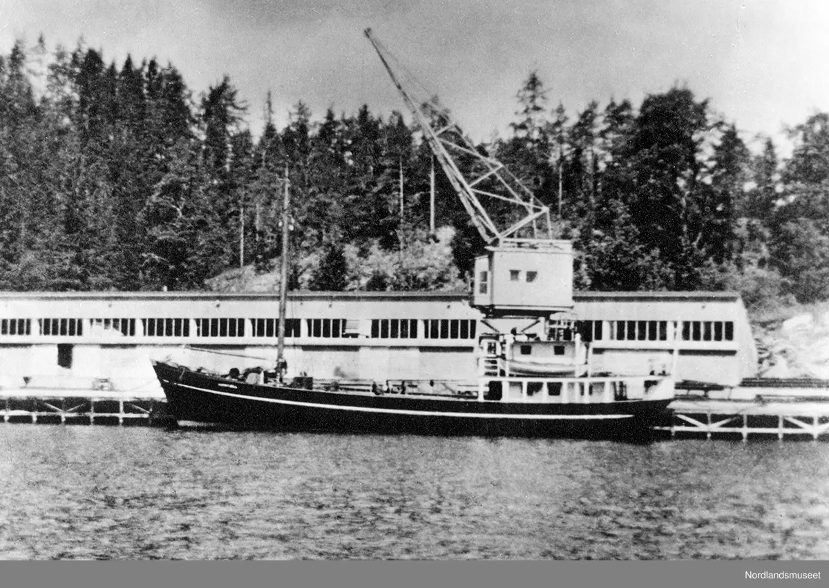 Frakteskuta "Havnfjell" ligger ved en kai i Forvik. Større bygning på ...