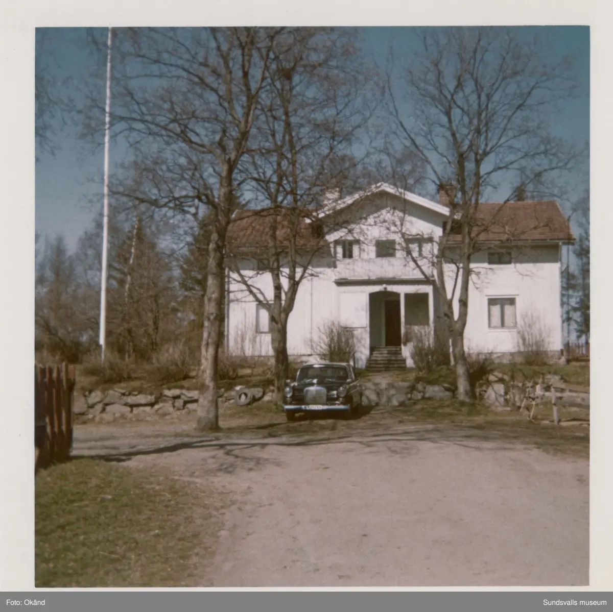 Vit mangårdsbyggnad med stenmur framför, en flaggstång och en svart ...