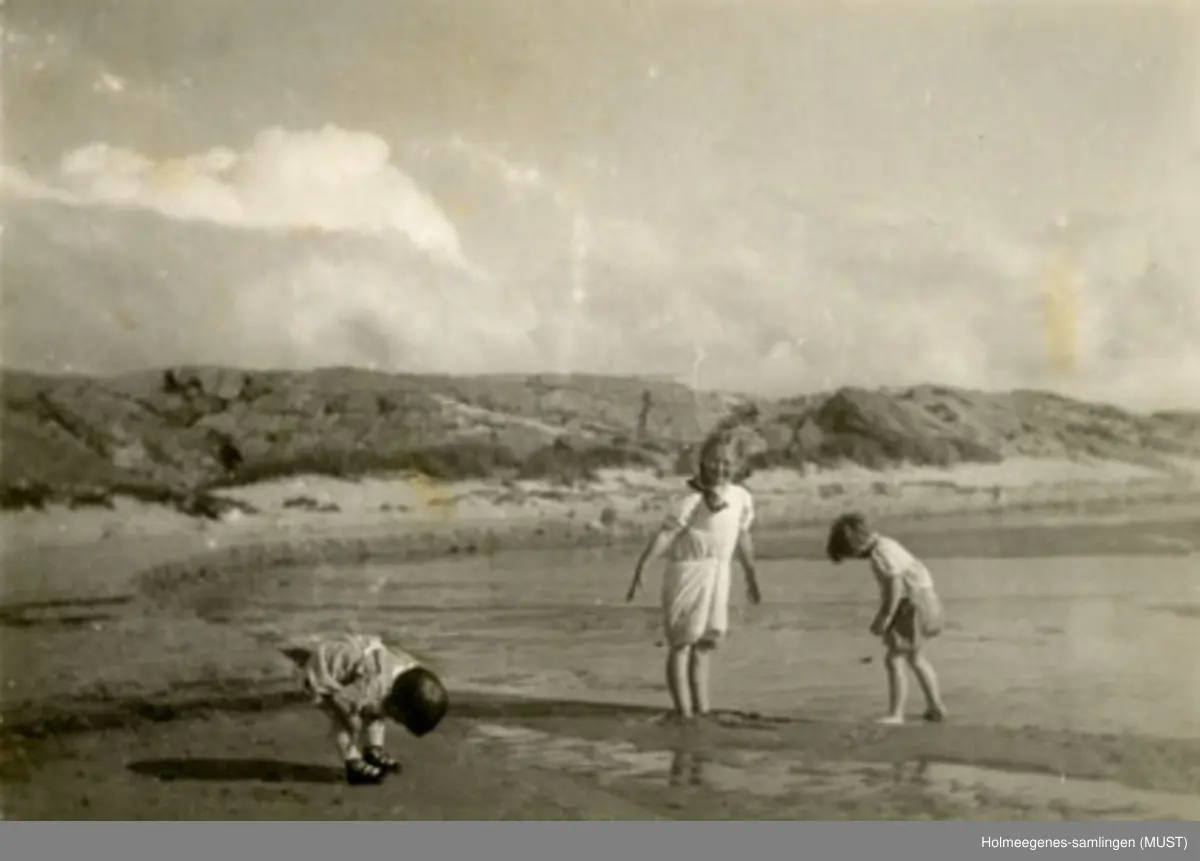 Tre små jenter leker på en strand med sanddyner eller svaberg i ...