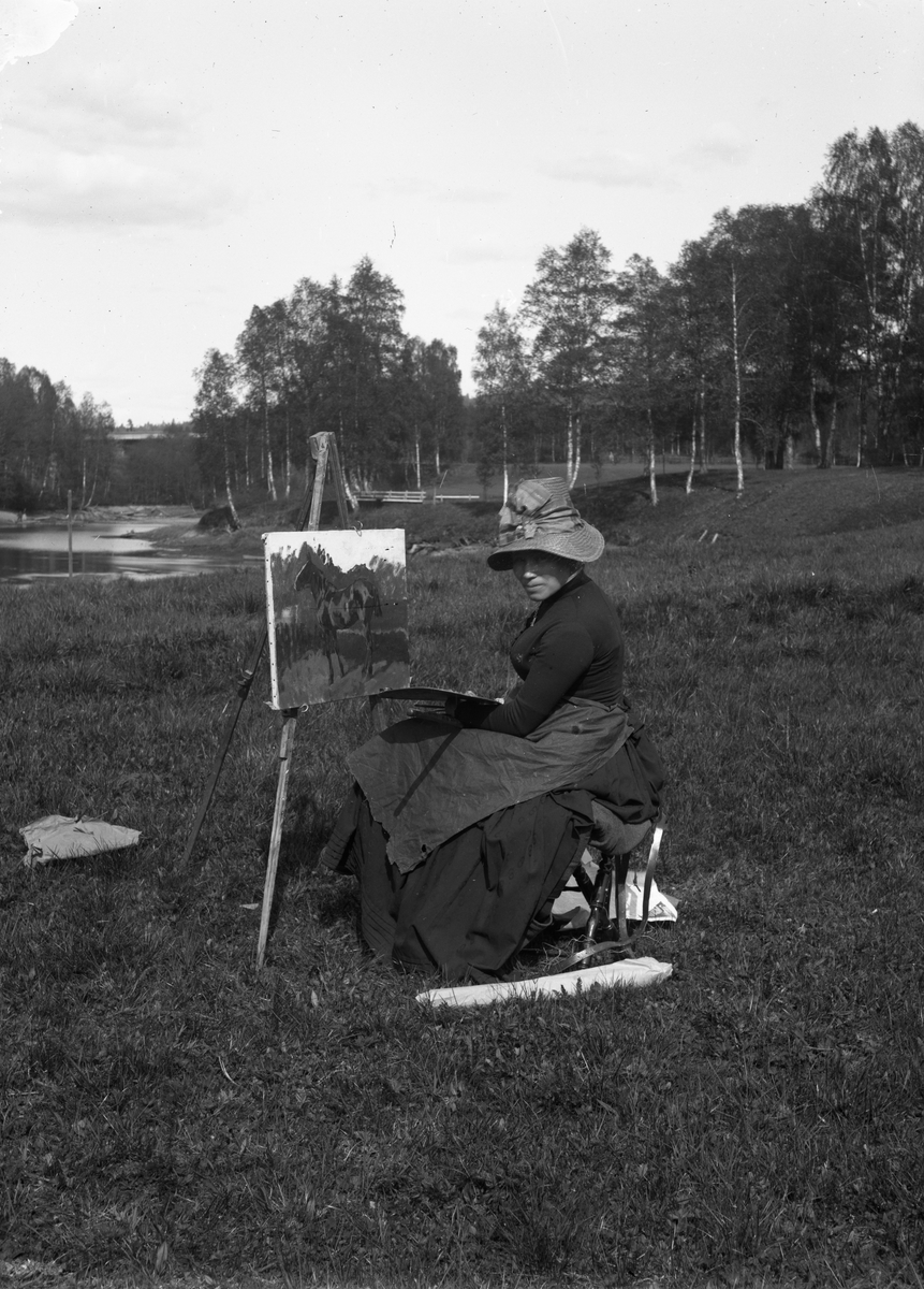 Portrett, malerinne Elisabeth Sinding, sittende med stor hatt utendørs ...