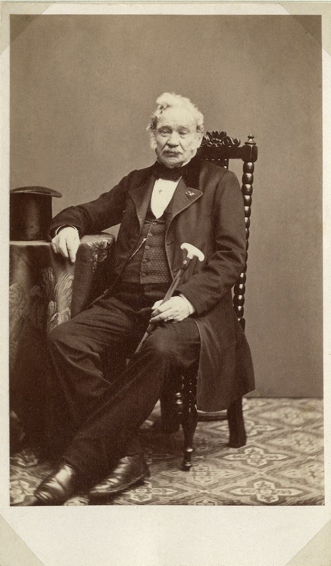 Porträttfoto av en äldre man i mörk redingot med mönstrad väst ...